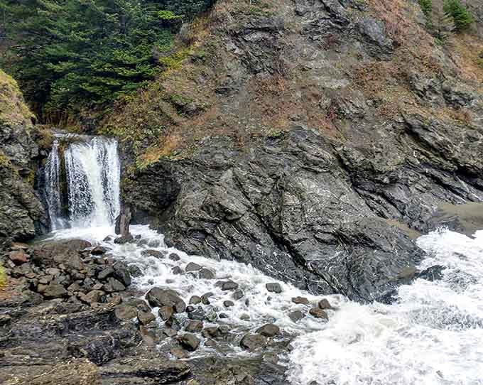 A small waterfall cascades over dark rocks, adding fresh water drama to this already spectacular coastal scene.