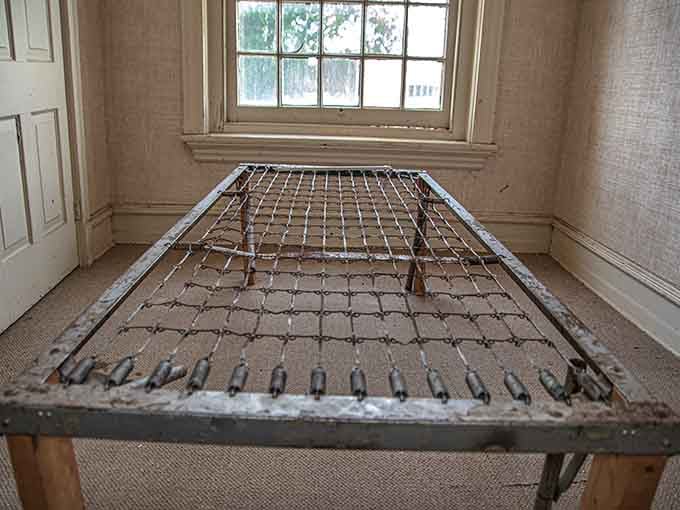 A metal bed frame stripped bare, leaving only springs and questions about who once tried to sleep here.