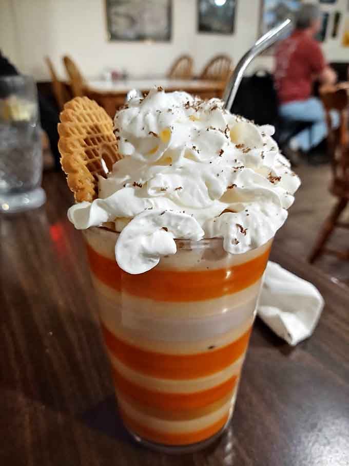 Layered dessert parfait topped with whipped cream and a wafer cookie looks like happiness served in a glass with a straw.