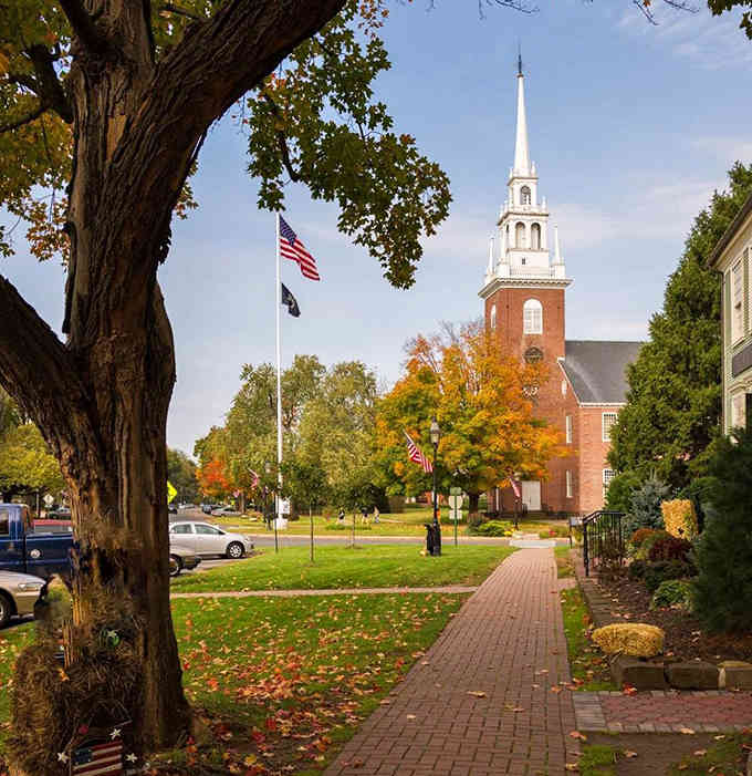 Autumn transforms the town green into a postcard, complete with that iconic white steeple reaching toward impossibly blue skies.