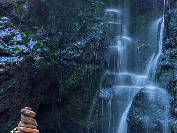A peaceful cairn sits sentinel beside the misty falls, where water seems to float down in slow motion.