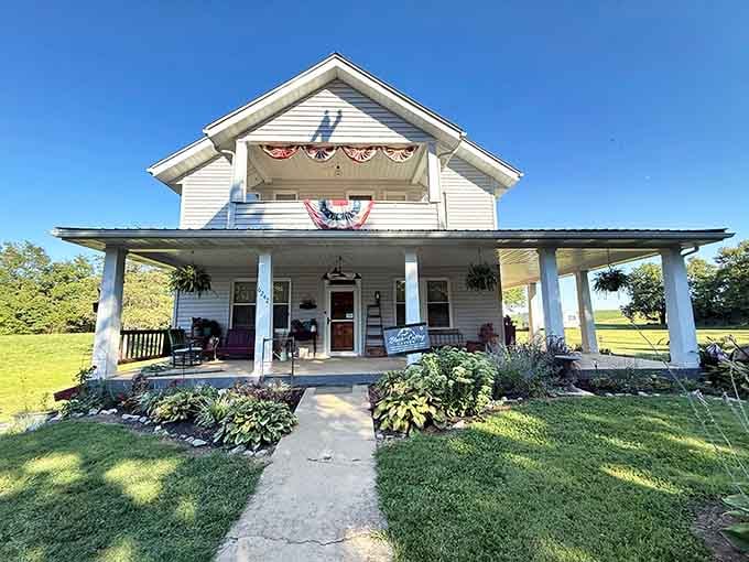 A charming farmhouse exterior welcomes adventurers, its patriotic bunting and wraparound porch concealing the geological marvel hidden below the property.