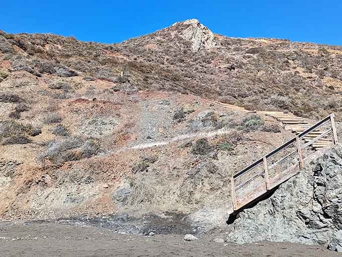 Wooden steps cling to the hillside, leading brave souls down to shores that defy typical beach expectations.