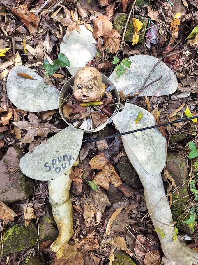 Vintage shovel blades bloom like metallic petals around a weathered doll face, transforming trash into treasure with remarkable creative vision.