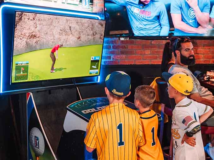 Young fans in matching jerseys huddle around a golf simulator, creating the next generation of sports bar enthusiasts right now.
