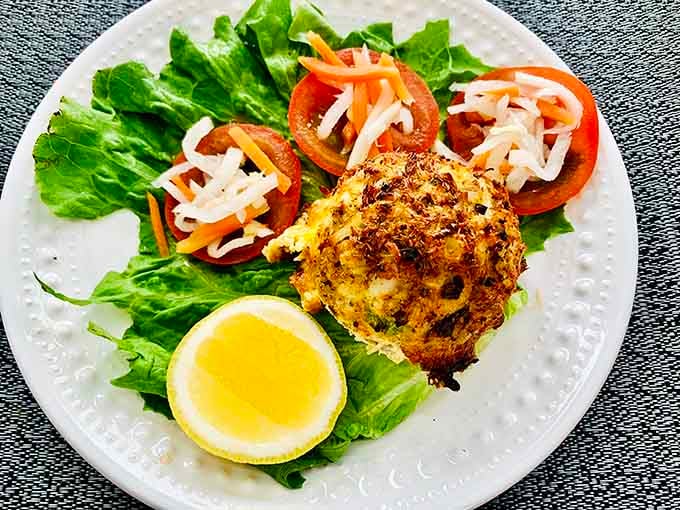 A crab cake so perfectly golden it could win a beauty pageant, nestled on fresh greens like edible treasure.