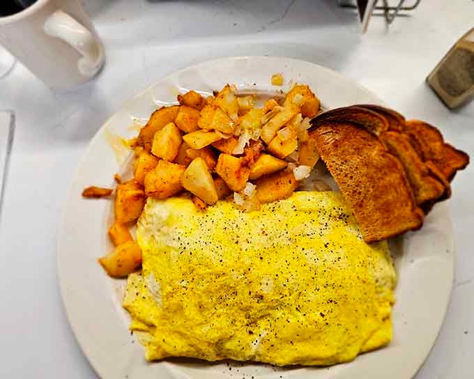 That fluffy yellow omelet with perfectly seasoned homefries and toast represents the holy trinity of diner breakfast done right.