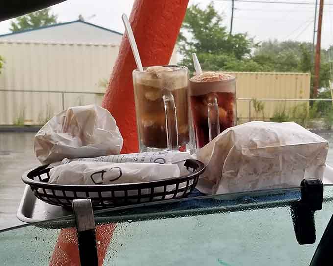 Root beer floats catching the afternoon light while rain dots the windshield: pure drive-in poetry in motion.