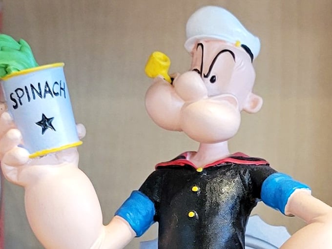 Popeye clutches his spinach can, forever frozen mid-gulp, his forearms as impressively oversized as his bobbling sailor head.