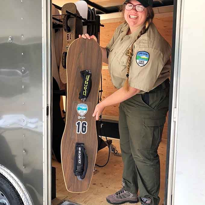 Your friendly ranger holds a sandboard like it's Excalibur, ready to guide you toward your next great adventure.