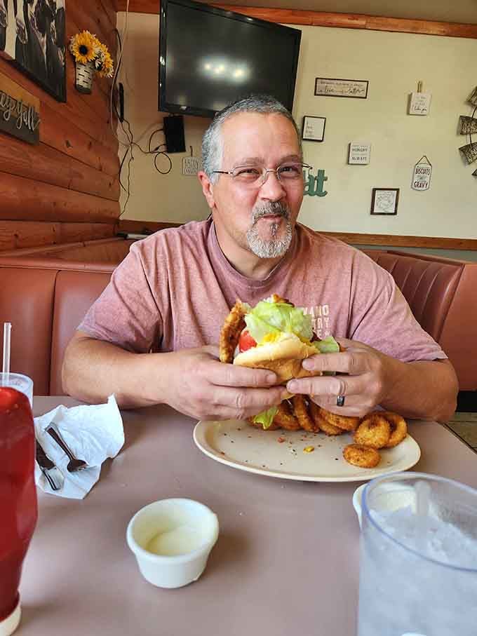 A satisfied customer enjoying what appears to be a tenderloin sandwich that requires both hands and serious commitment.