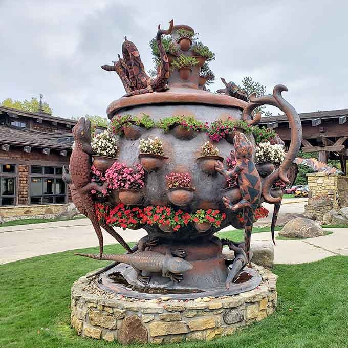 A fantastical teapot fountain covered in creatures and flowers greets visitors with whimsical charm outside the entrance.