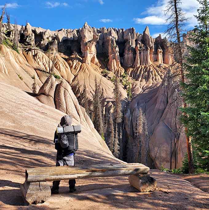 One hiker contemplates the view from a wooden bench, dwarfed by geological giants that put human scale into perspective.