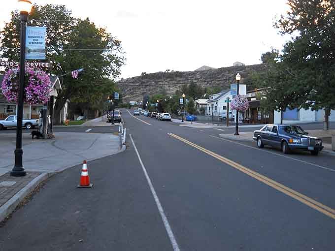 Daylight bathes the street in golden warmth while hanging baskets add splashes of purple to the scene.