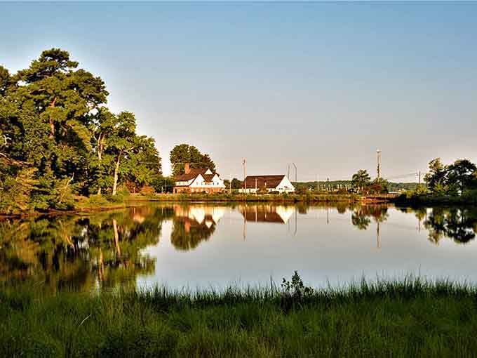 Golden light bathes the shoreline where trees and buildings mirror themselves in water smooth as glass on Sunday morning.
