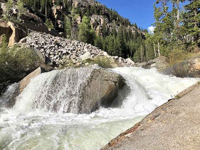Rushing water cascades over smooth rocks along the trail, offering nature's own soundtrack for mountain adventures.