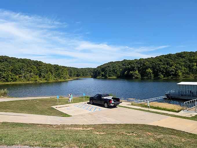 The boat launch beckons adventurers while forested hills embrace the water like protective arms welcoming you home.