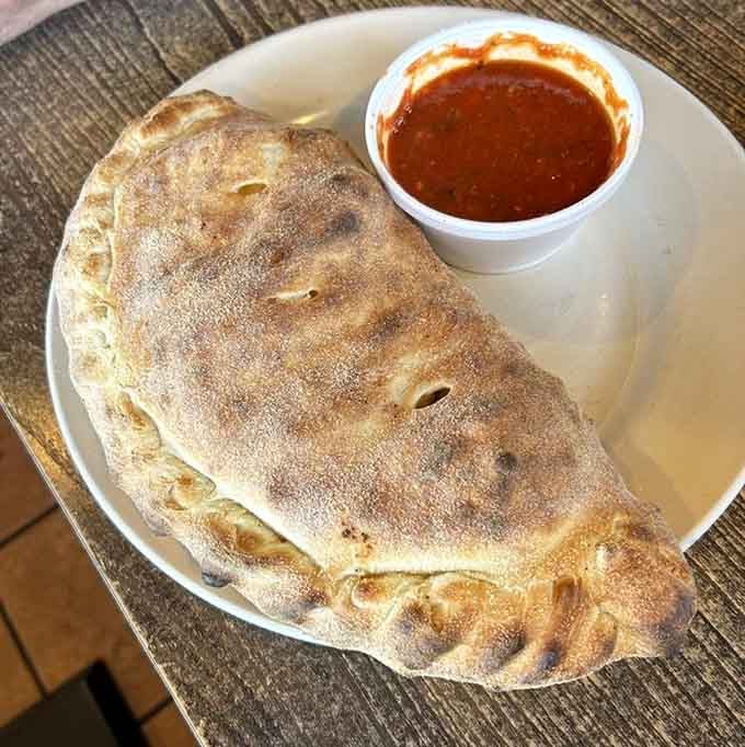 That golden calzone arrives stuffed with fillings and paired with marinara for dipping like it should be.