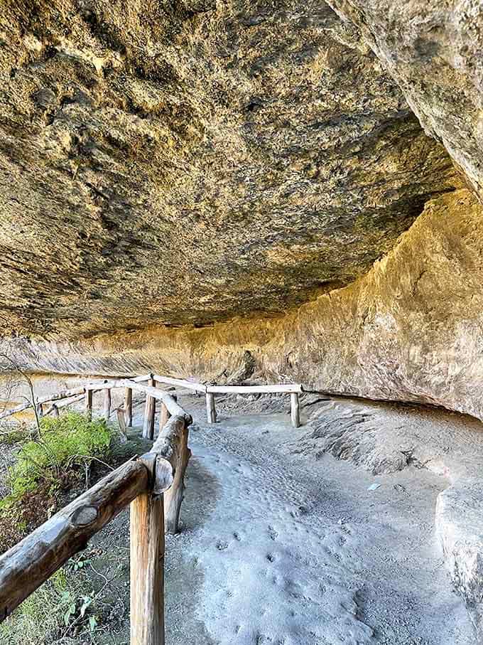 The trail winds beneath that massive overhang, where millions of years of geological history are written in stone layers.