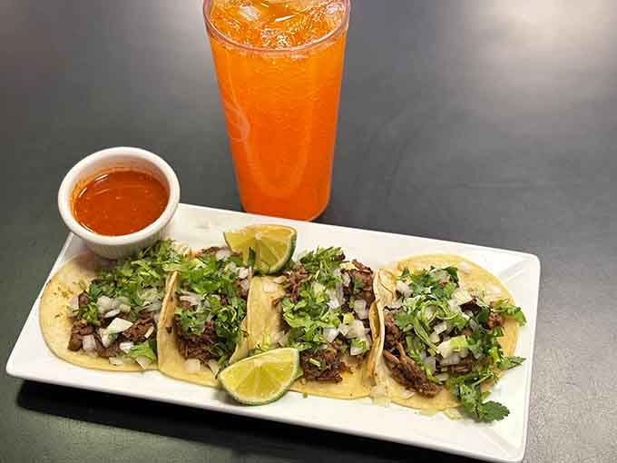 Tender shredded beef tacos topped with fresh cilantro and onions, served with lime wedges and bright orange agua fresca.