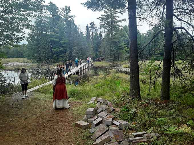 Period-dressed visitors cross the wooden bridge, stepping into a world where Wisconsin wilderness meets medieval wonder perfectly.