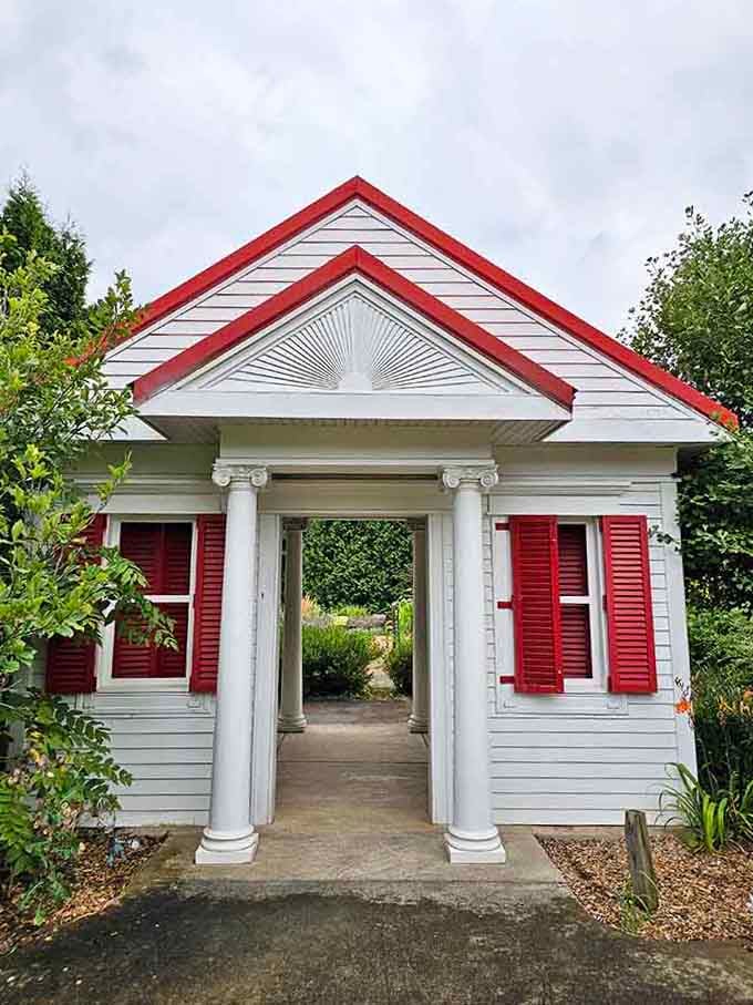 Red shutters and white columns frame a garden gateway that makes every entrance feel like stepping into something special.