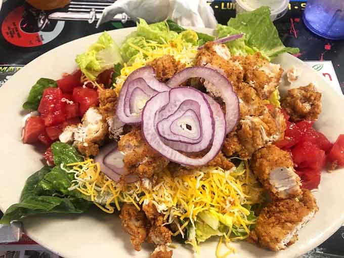Crispy fried chicken crowning a fresh salad with red onion rings, proving healthy eating can still be indulgent and fun.