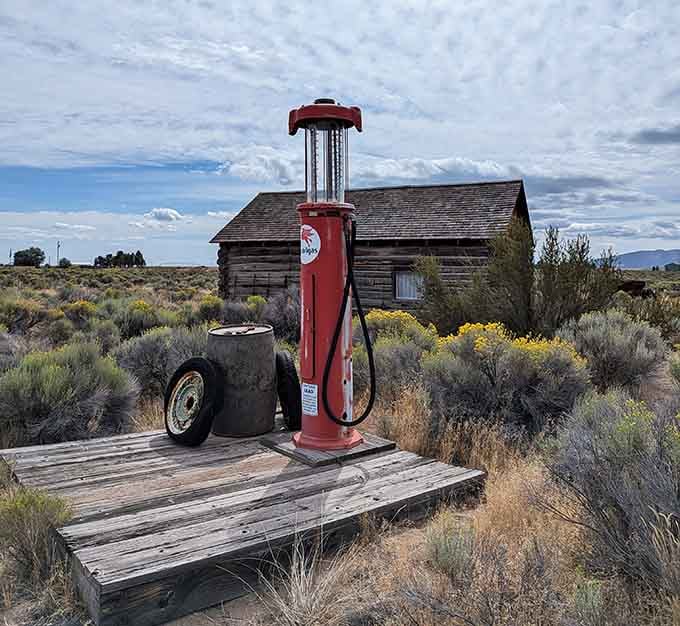 A vintage red gas pump stands sentinel by a weathered cabin, back when filling up meant actual human interaction.