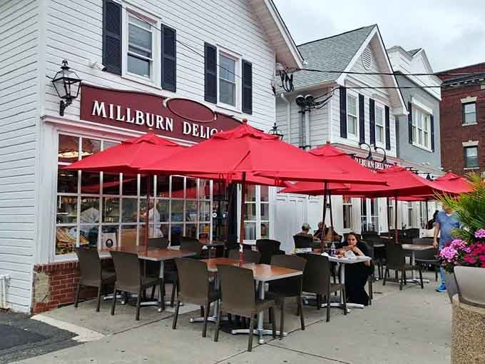 Red umbrellas create a cheerful canopy where outdoor diners enjoy their sandwiches while watching the world stroll past contentedly.