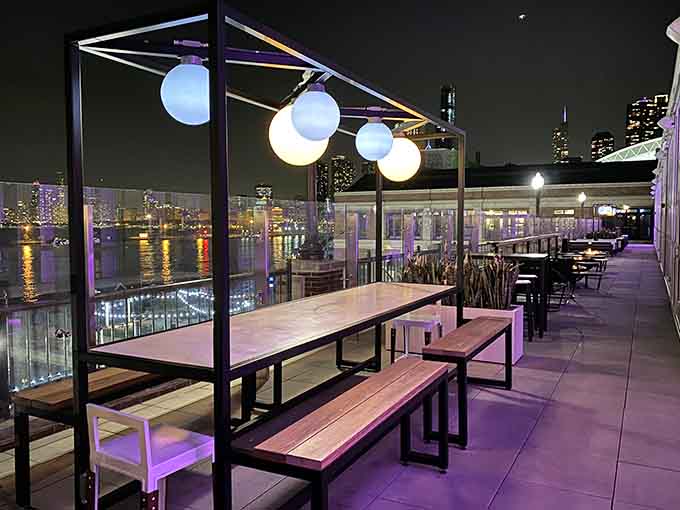 The outdoor terrace at night transforms into an illuminated escape where city lights dance on the water below you.