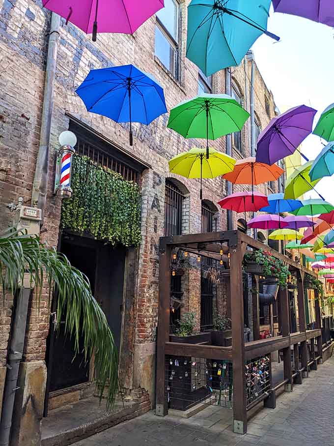 The charming brick buildings and lush greenery create the perfect backdrop for this whimsical umbrella installation that transforms an ordinary alleyway.