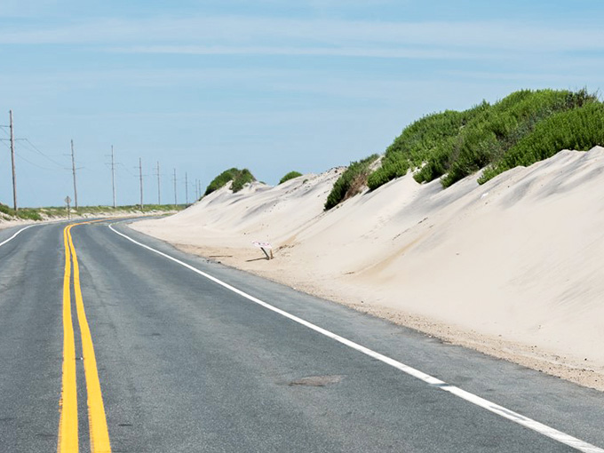 The perfectly paved highway cuts through sand dunes that could reclaim it tomorrow if they felt like it.