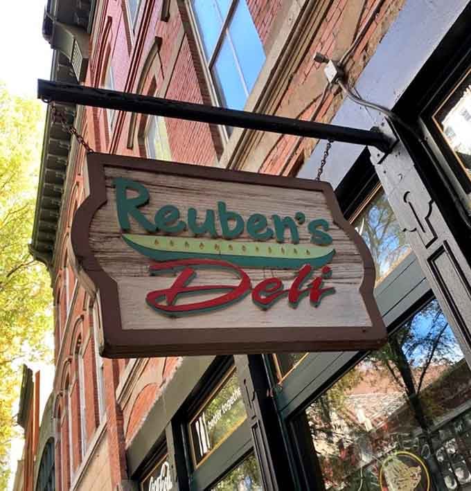 That vintage-style sign swinging above the sidewalk whispers promises of overstuffed sandwiches and old-school deli excellence.