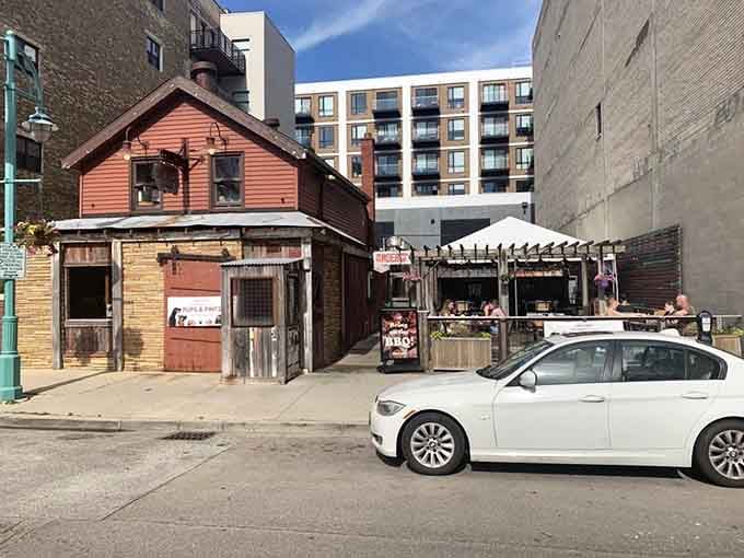 A tiny wooden shack surrounded by modern buildings, standing proud like a delicious middle finger to corporate conformity.