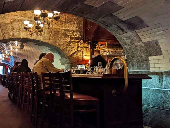 The bar glows like a wooden altar where skilled bartenders perform nightly miracles with spirits, bitters, and flair.
