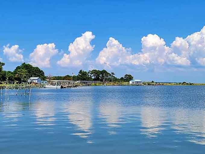 Puffy clouds drift over calm water that reflects the sky like someone polished it just for your visit today.