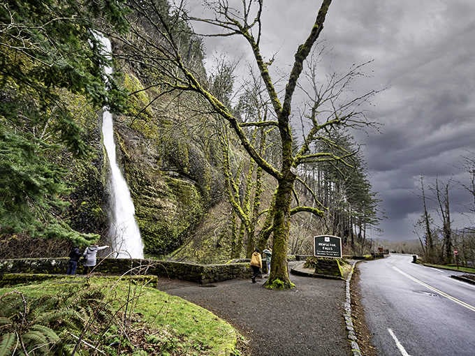 Moss-draped trees frame a waterfall that drops like nature's own curtain call along this historic engineering marvel.