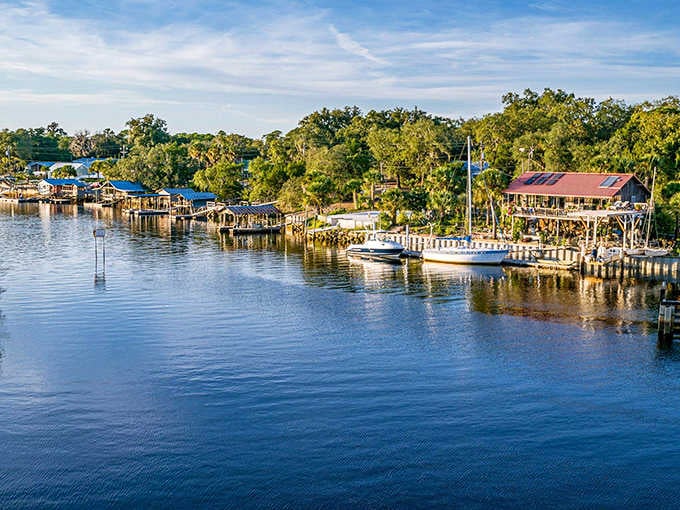 Golden hour transforms these riverside docks into a postcard, where fishing boats rest peacefully beneath towering trees.