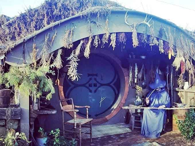 Cozy hobbit cottage charm surrounds you as you relax beside a wizard figure under a leafy roof doorway glowing warmly.