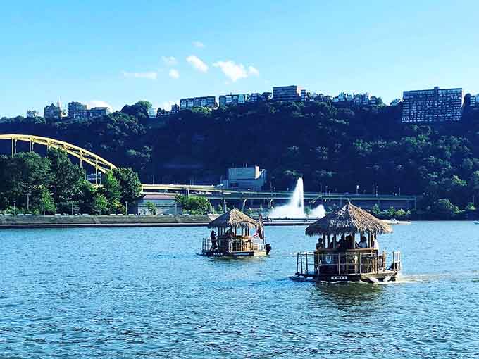 Two tiki boats cruising together because even floating tropical bars need friends, with Point State Park's fountain providing the backdrop.