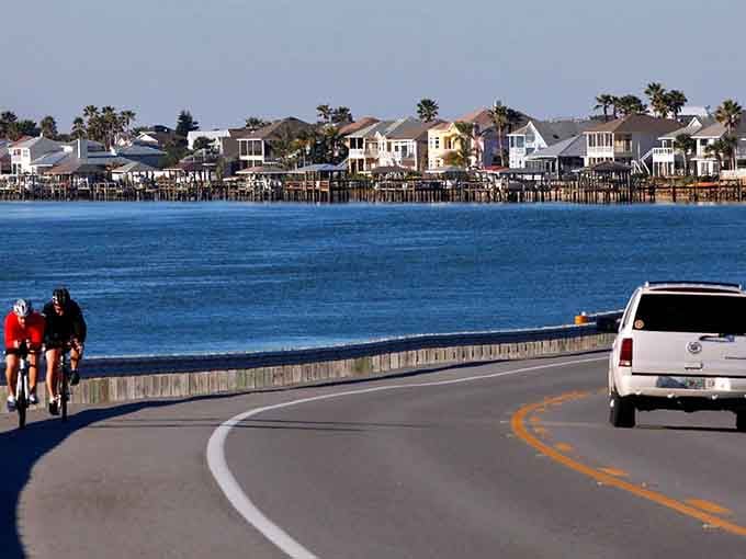 Cyclists and drivers share this waterfront road where blue skies meet bluer waters and waterfront homes dot the horizon.
