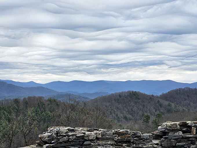 Those rippling cloud formations above the misty mountain layers look like something from a Bob Ross painting come to life.