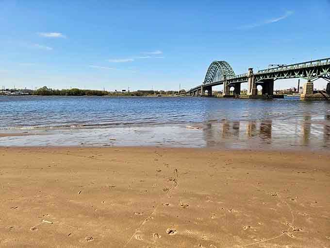The Tacony-Palmyra Bridge watches over sandy shores where river meets land in timeless beauty.