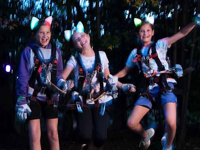 Pure joy captured mid-adventure: three friends discovering that happiness really does glow in the dark at treetop level.