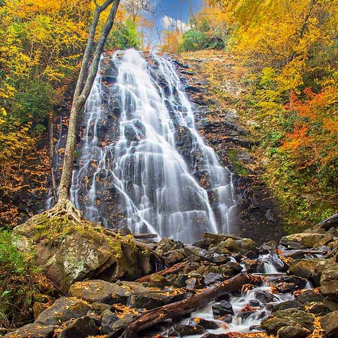Autumn paints this towering waterfall with nature's most vibrant palette of gold, orange, and crimson leaves all around.