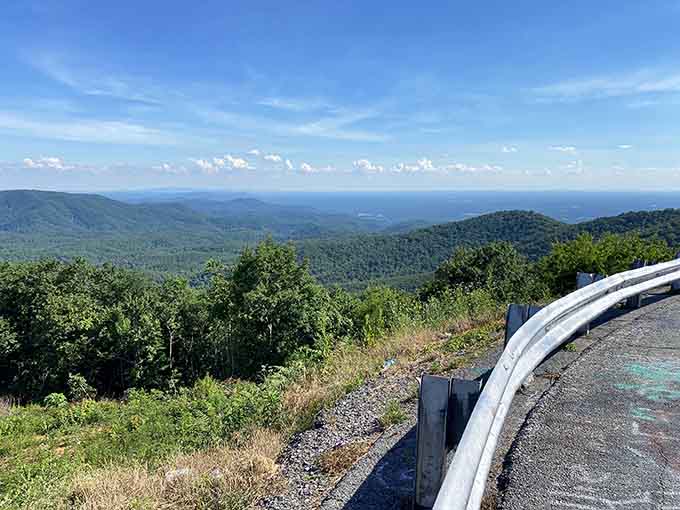 That guardrail curves along the roadside where forest-covered peaks fade into misty blue layers stretching toward forever.