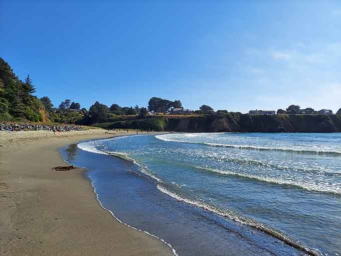 Gentle waves roll onto pristine sand where beachcombers search for treasures beneath dramatic coastal bluffs.