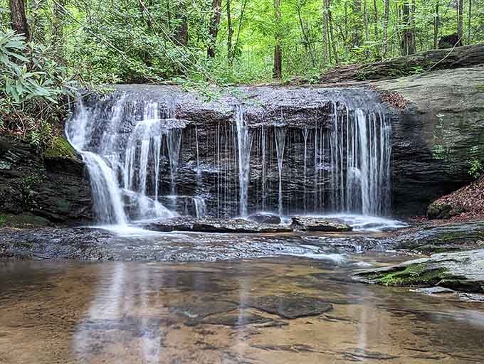 Water spreads across the rock face like nature's own beaded curtain, creating a peaceful cascade worth every step.