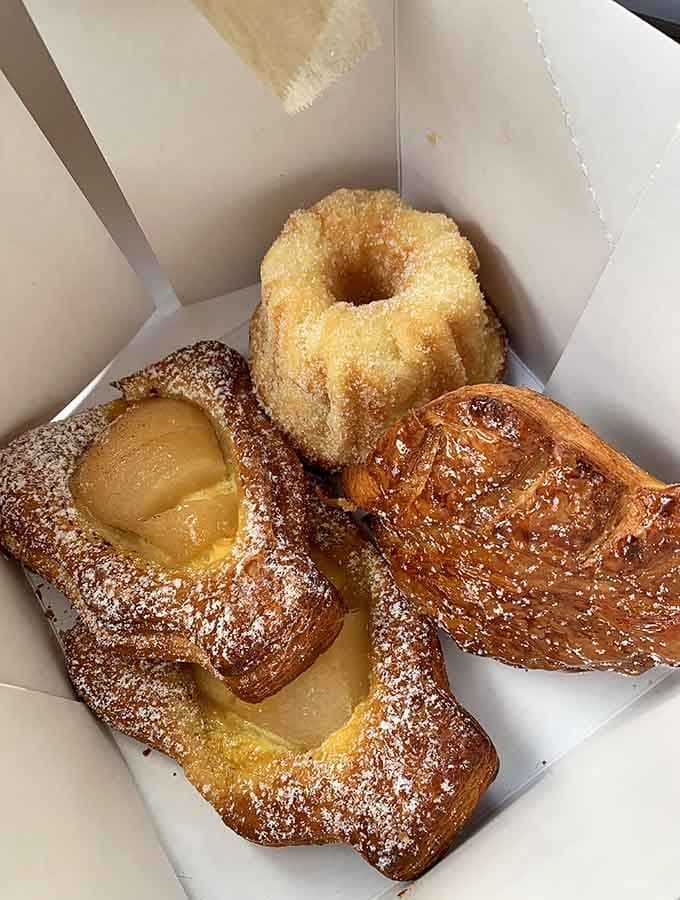 Three pastries walk into a box: a Danish, a kouign-amann, and pure temptation wrapped in powdered sugar.