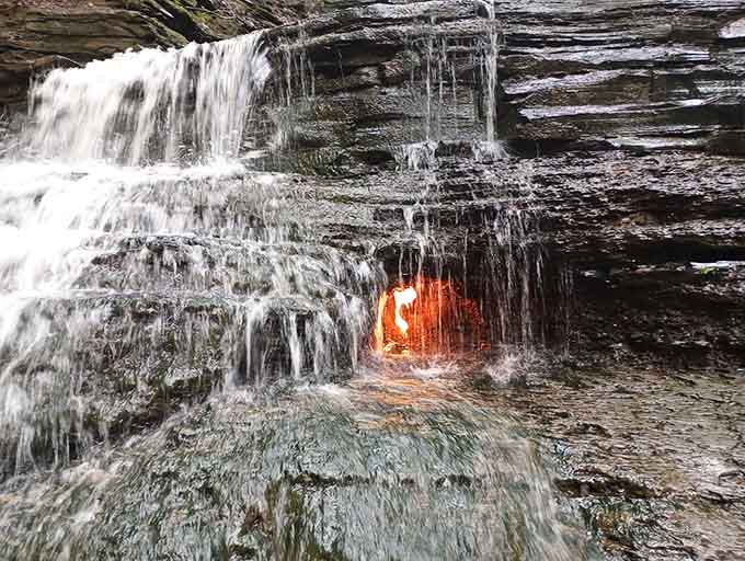 Watch the water veil part to reveal nature's best-kept secret, burning bright in its rocky alcove sanctuary.